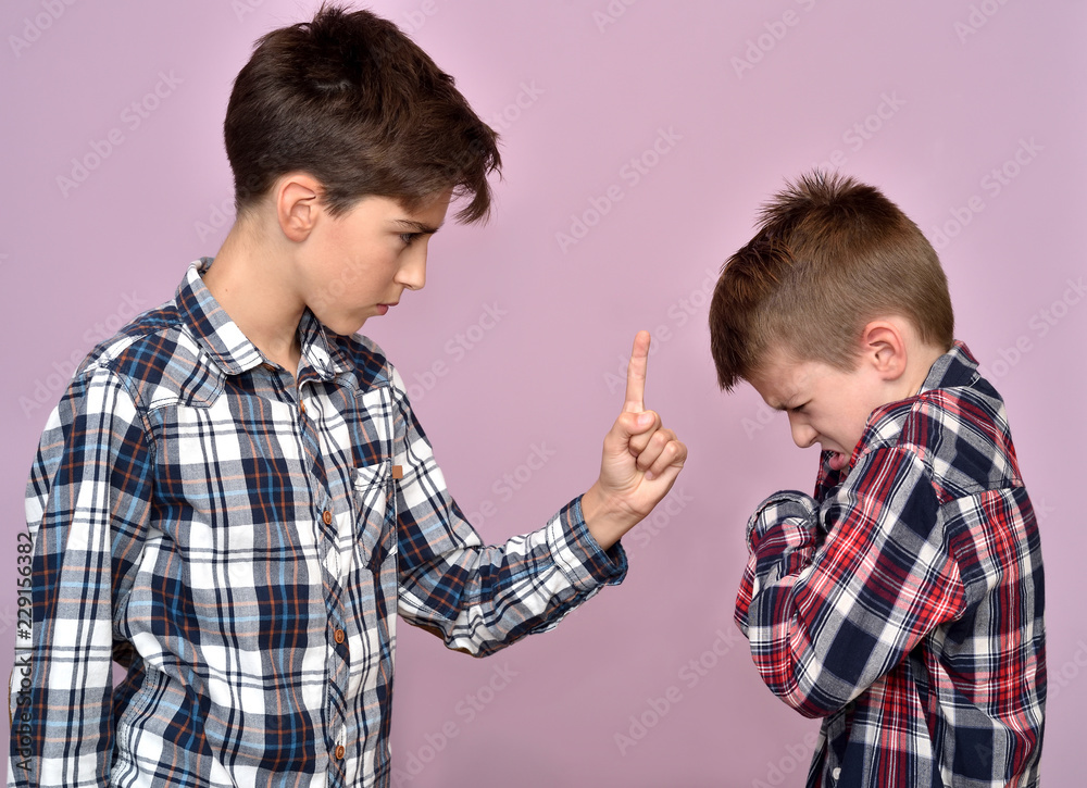 Angry young boy with index fingers up scolding a scared little brother ...