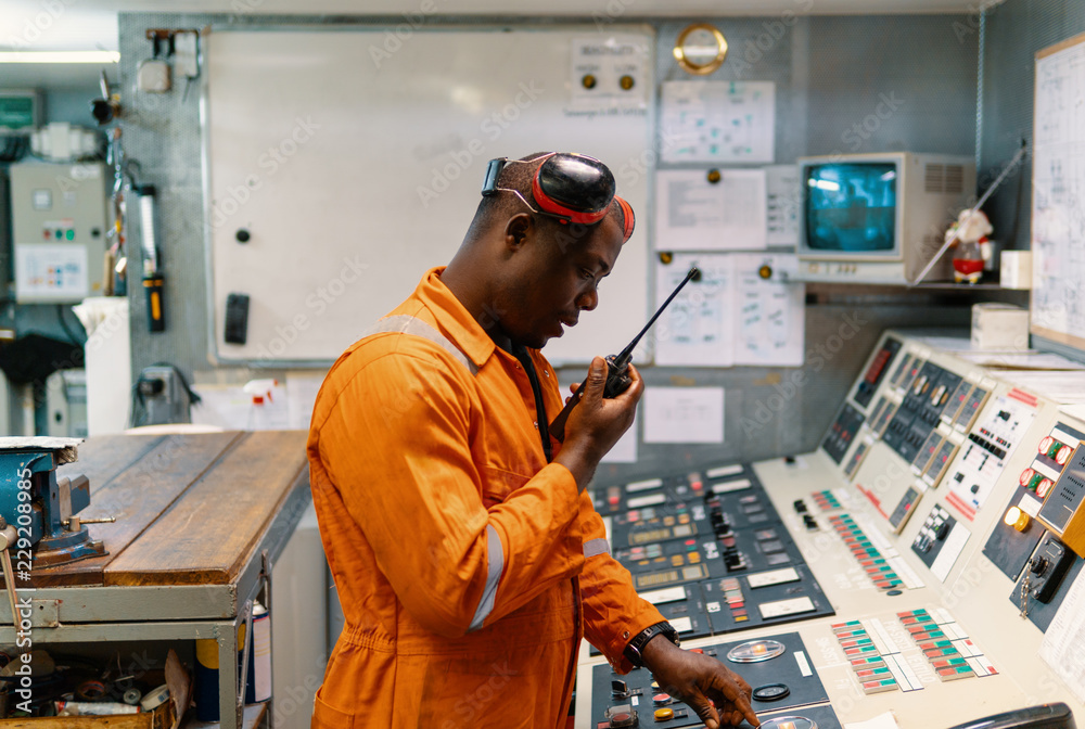 African marine engineer officer in engine control room ECR. He speaks ...