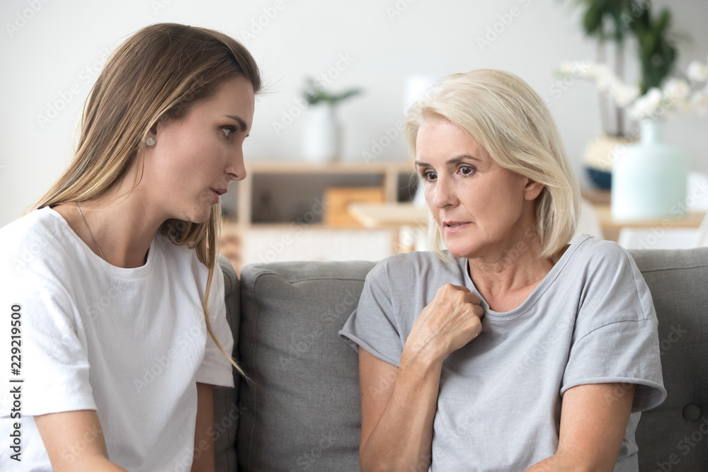 Concerned aged mother and adult daughter sit on couch having serious ...
