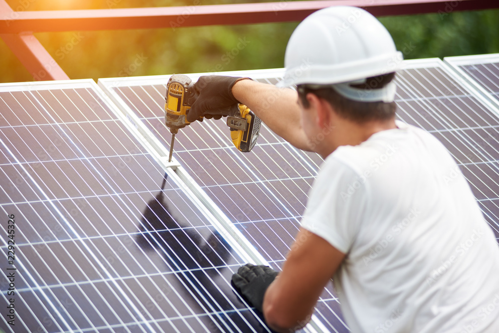 Back view of young technician in helmet connecting solar photo voltaic ...