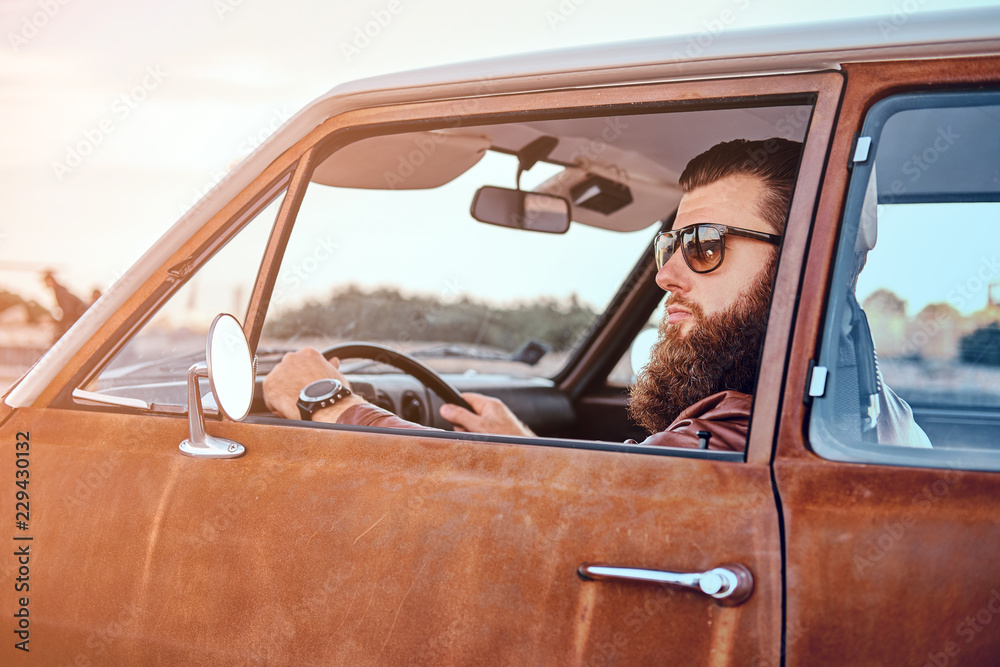 Bearded male in sunglasses dressed in brown leather jacket driving a ...