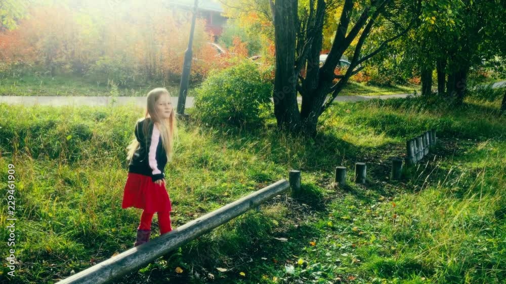 Little girl walking on a balance beam in a park on a beautiful autumn ...