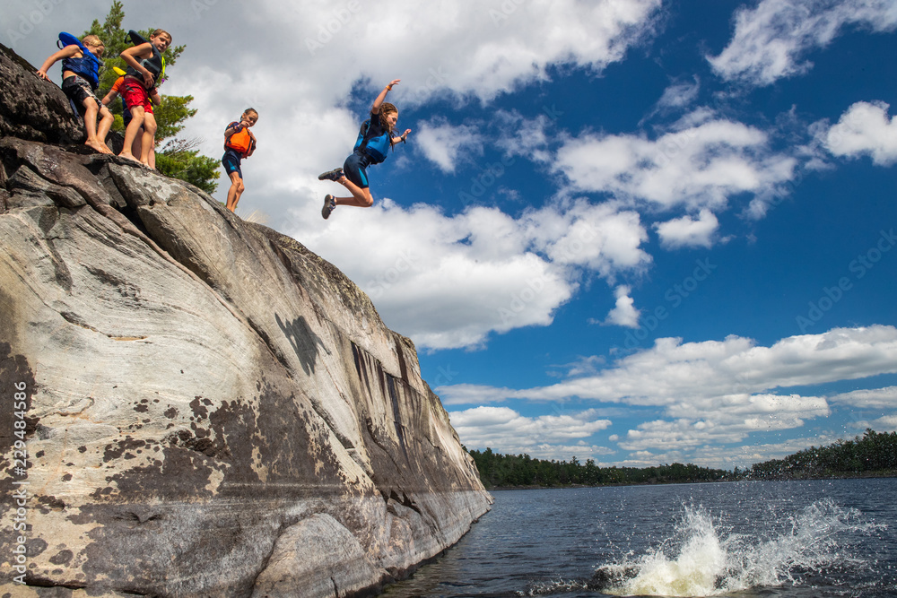 Kids jumping off cliffs while on a canoe trip Stock Photo | Adobe Stock