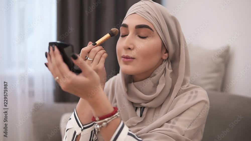 Muslim woman doing makeup on her face with brush. Modern life of muslim ...