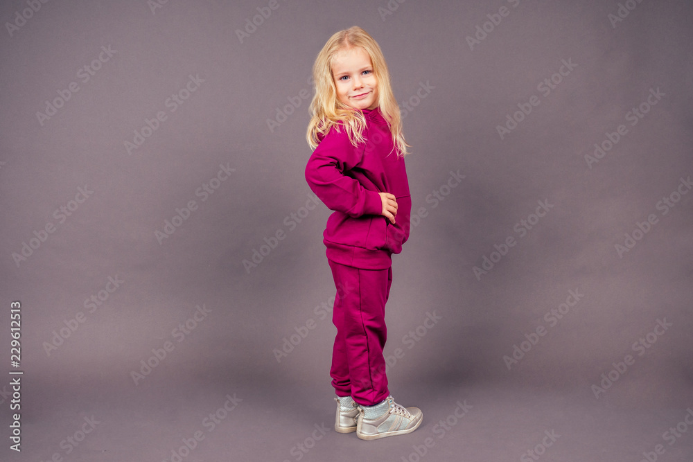 blonde blue-eyed little model girl in a purple sports suit posing in ...