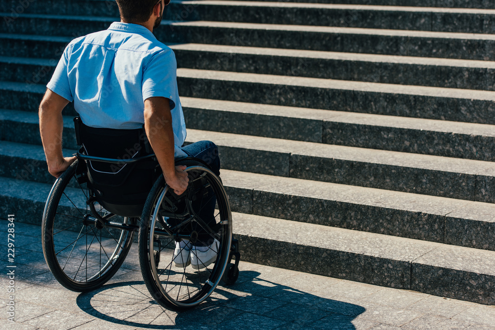 back view of disabled man using wheelchair on street and stopping near ...