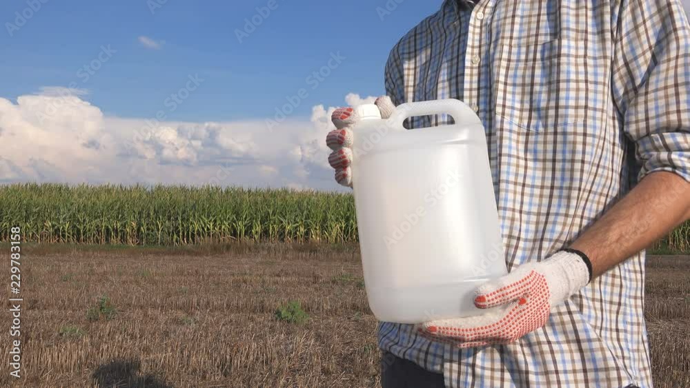 Farmer holding pesticide chemical jug in cornfield. Blank unlabeled ...