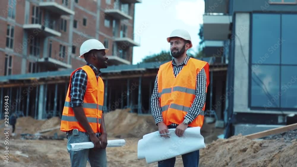 Two multiracial construction workers in safety helmets holding the ...