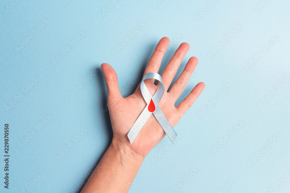 Helping hand holding blue ribbon awareness with red blood drop on a ...