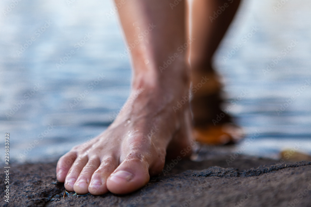 Young woman walking out of the water bare feet on a rock - Closeup ...