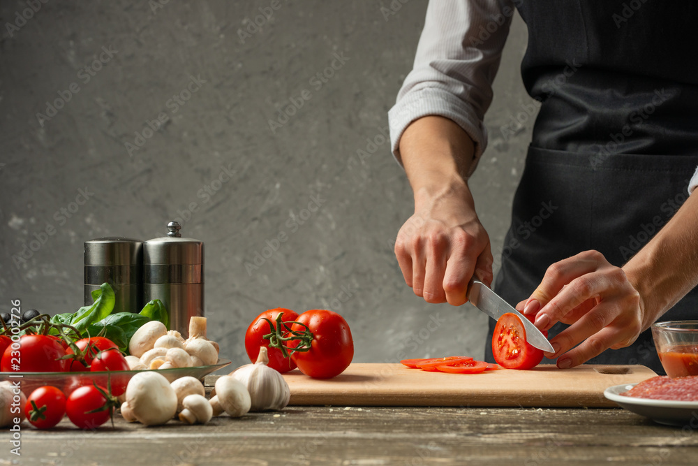 The concept of nutrition. The chef cuts tomatoes on the background of a ...