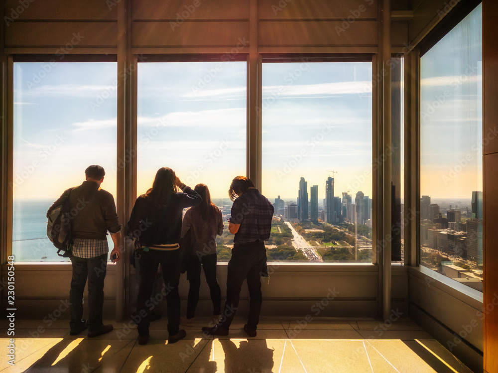 Group of visitors looking out of a skyscraper window. Chicago skyline ...