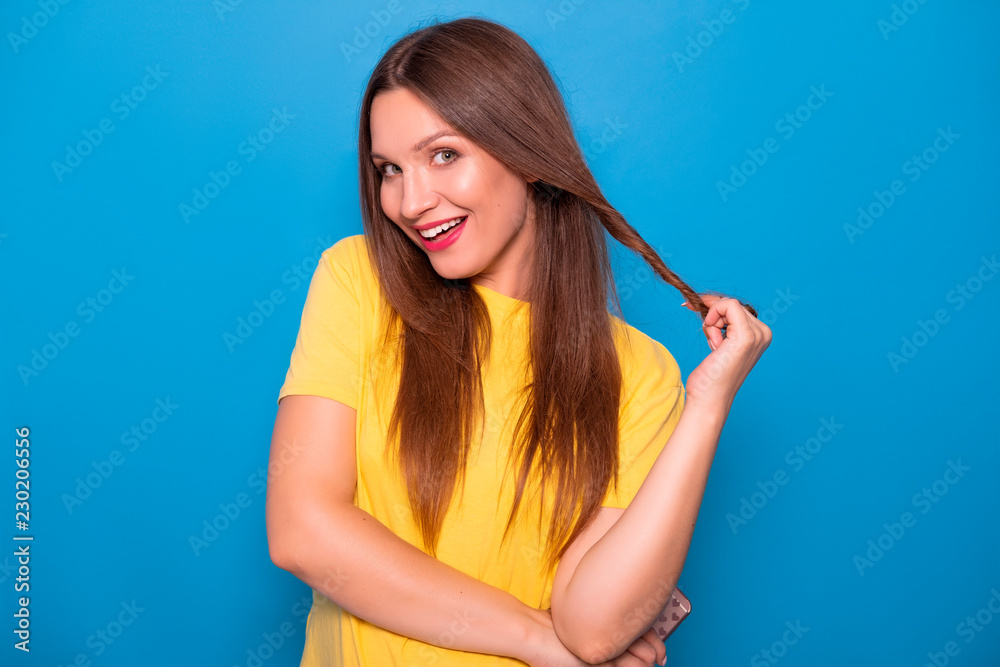 Cute brunette woman with long hair posing in yellow t-shirt on a blue ...