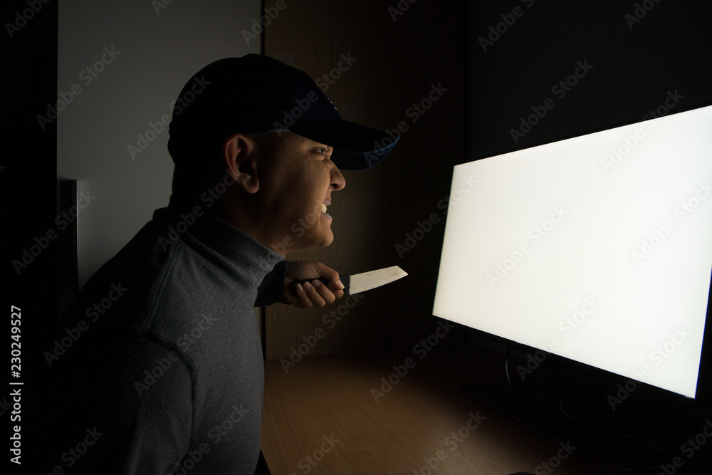 Side view of man Hacker sit at the computer monitor and hold the knife ...