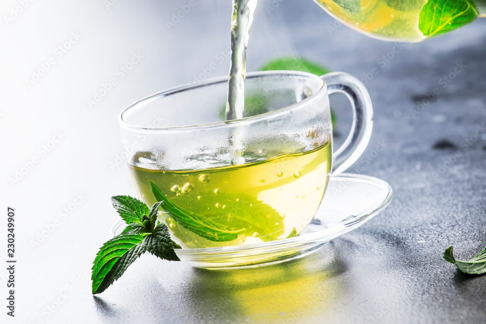 Hot chinese green tea with mint, with splash pouring from the kettle ...