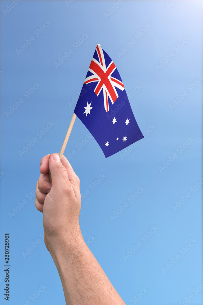 Hand holding Australia flag high in the air, with a clear blue sky ...