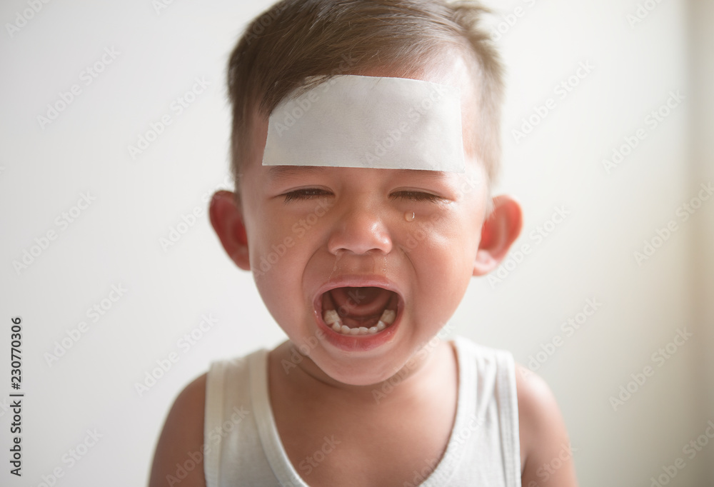 The cute little boy is crying while getting sick. Using a cool fever ...