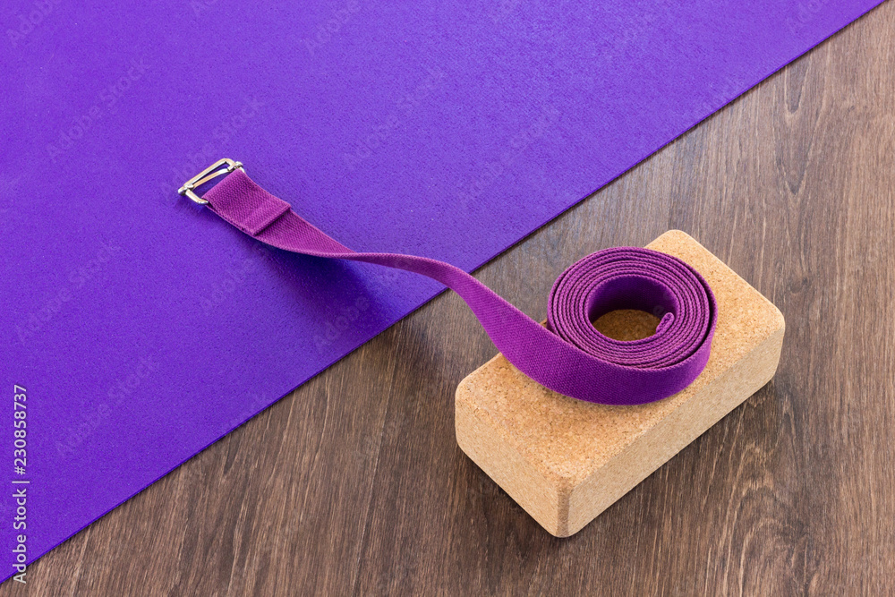 Purple mat unfolded on wooden floor next to cork block and strap on top ...