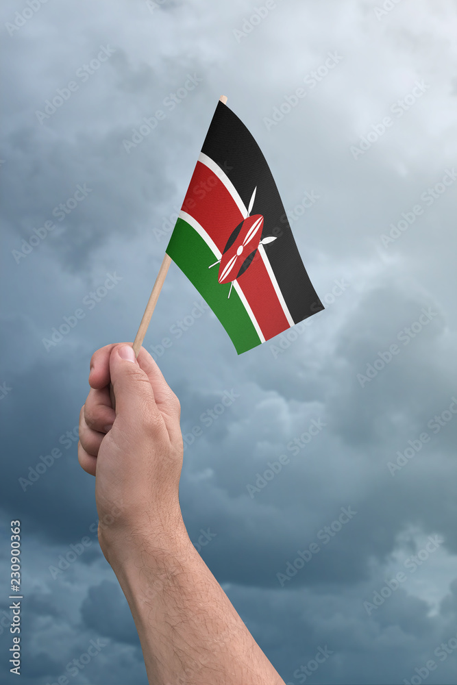 Hand holding Kenya flag high in the air, with a stormy, cloudy sky ...