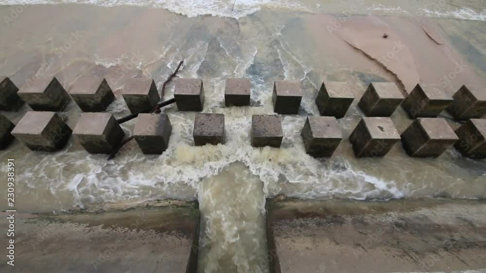 Water flows down over the spillway of a small concrete dam to the sea ...