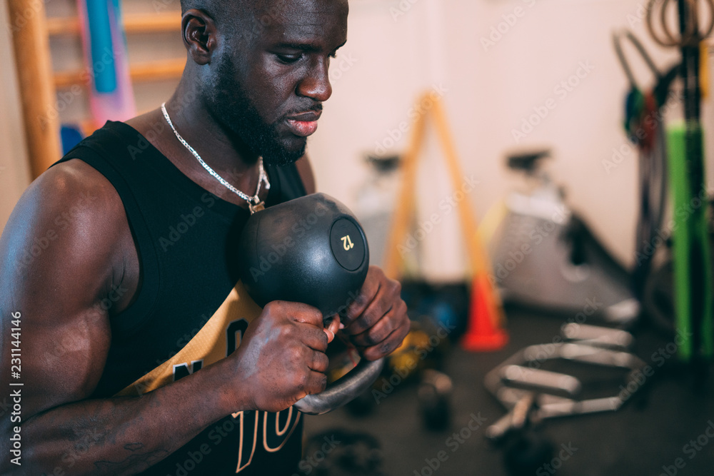 Black young muscular man training with kettlebell at gym. Strength and ...