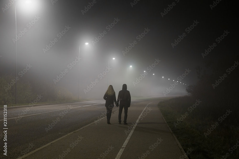 Young couple holding each other hands. Slowly walking under white street lights in night. Dark ...