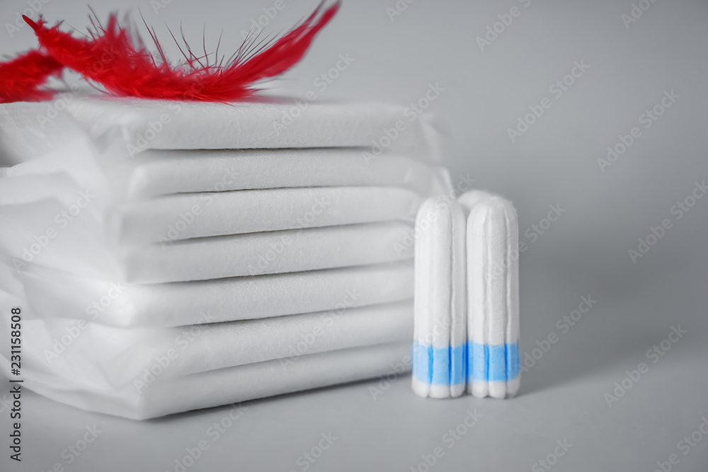 Stack of menstrual pads with tampons and red feathers on grey ...