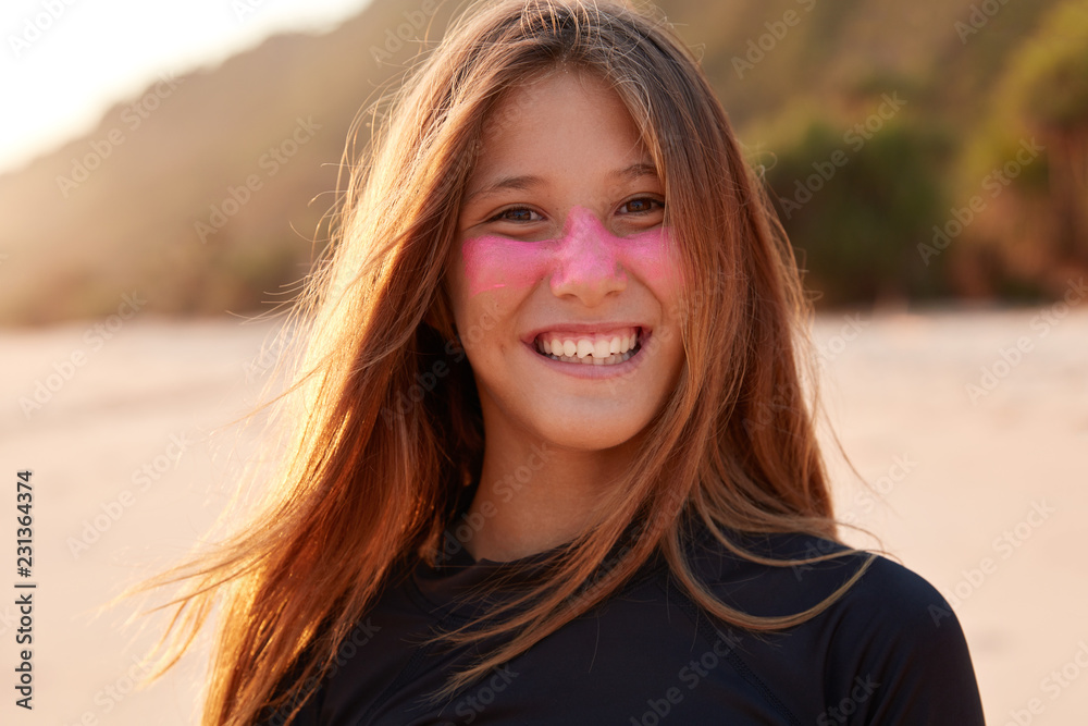 Close up shot of pretty woman with surf zinc on cheeks, smiles broadly ...