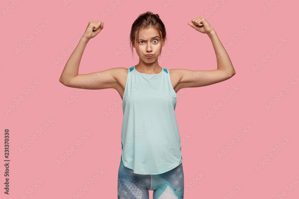 Photo of healthy sportive woman shows biceps and muscles, raises hands ...