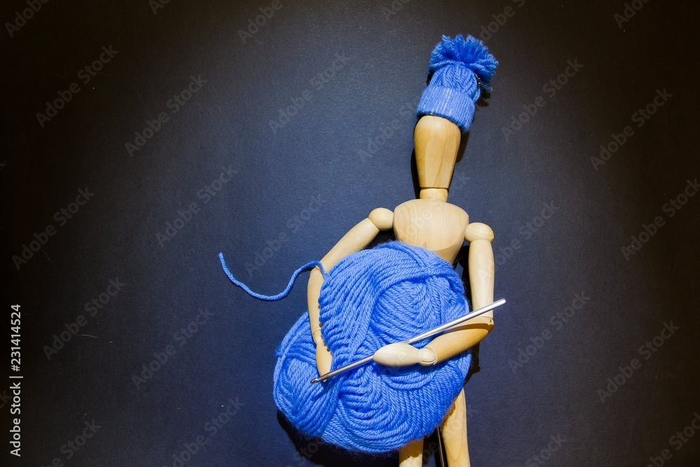 Wooden puppet doll holds a ball of blue yarn and crochet hook in its ...