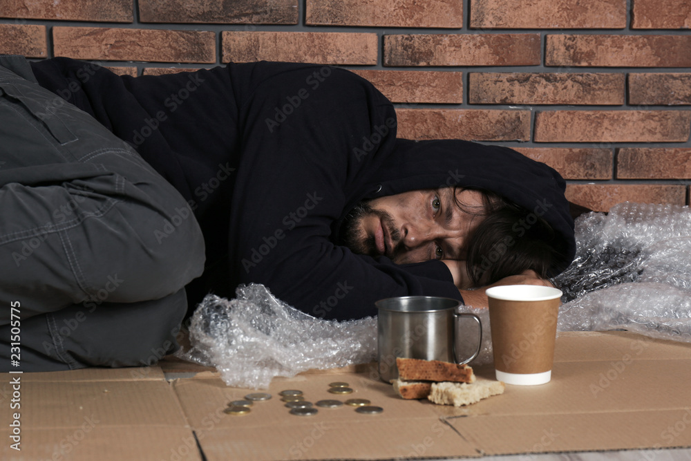 Foto de Poor homeless man lying on floor near brick wall do Stock ...