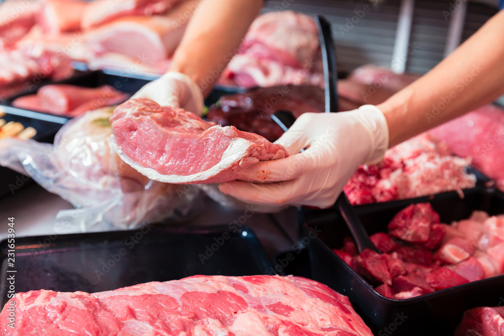 Poster Meat in a butcher shop display being put in by sales woman ...