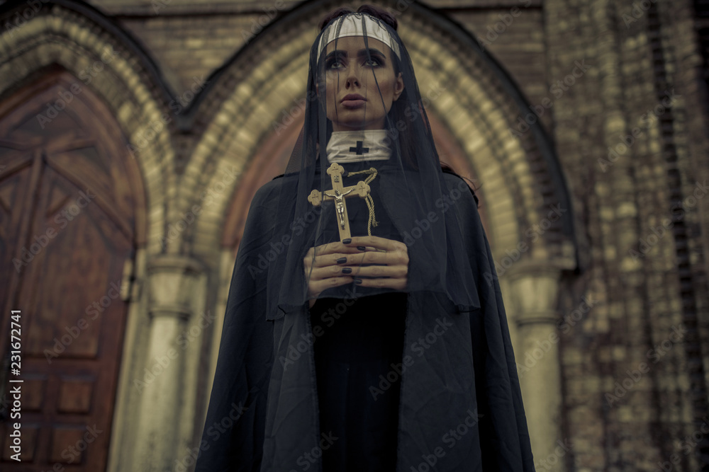 Young nun is standing and praying with cross in her hands on temple ...