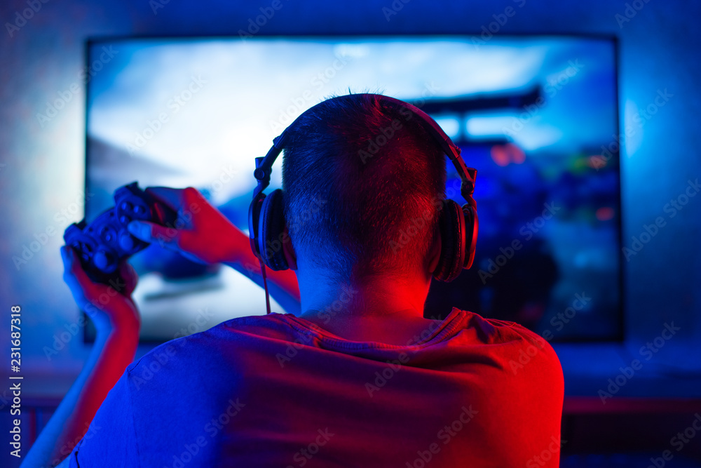 Rear view of a young player playing video games on an FPS console at ...