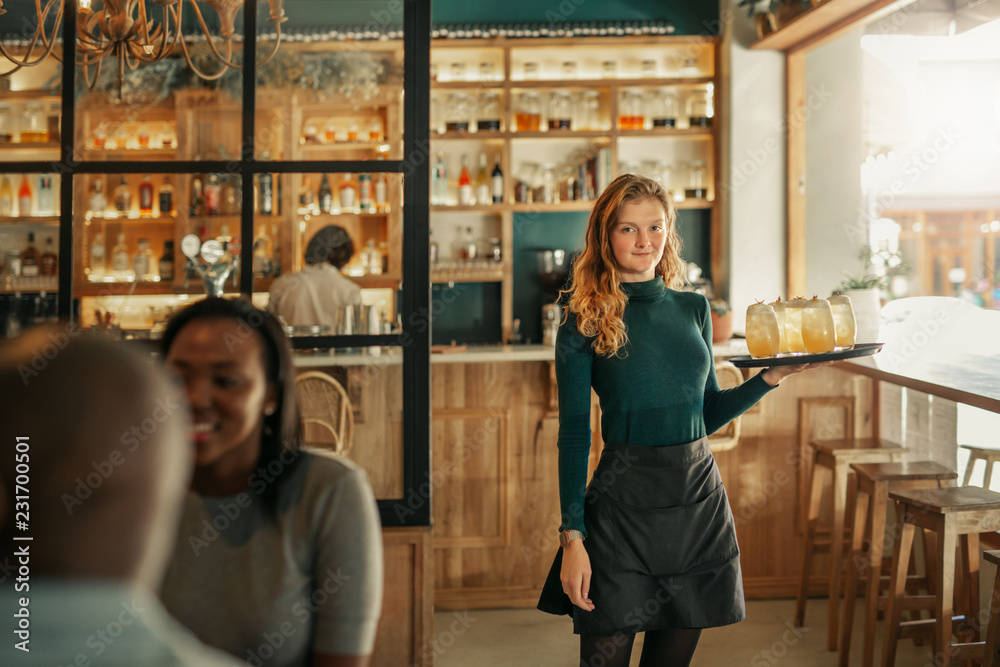 Smiling bar waitress standing with a tray of drinks Stock Photo | Adobe ...