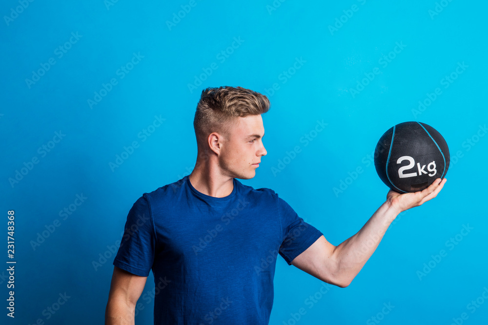 Portrait of a young man holding a heavy ball in one hand in a studio ...