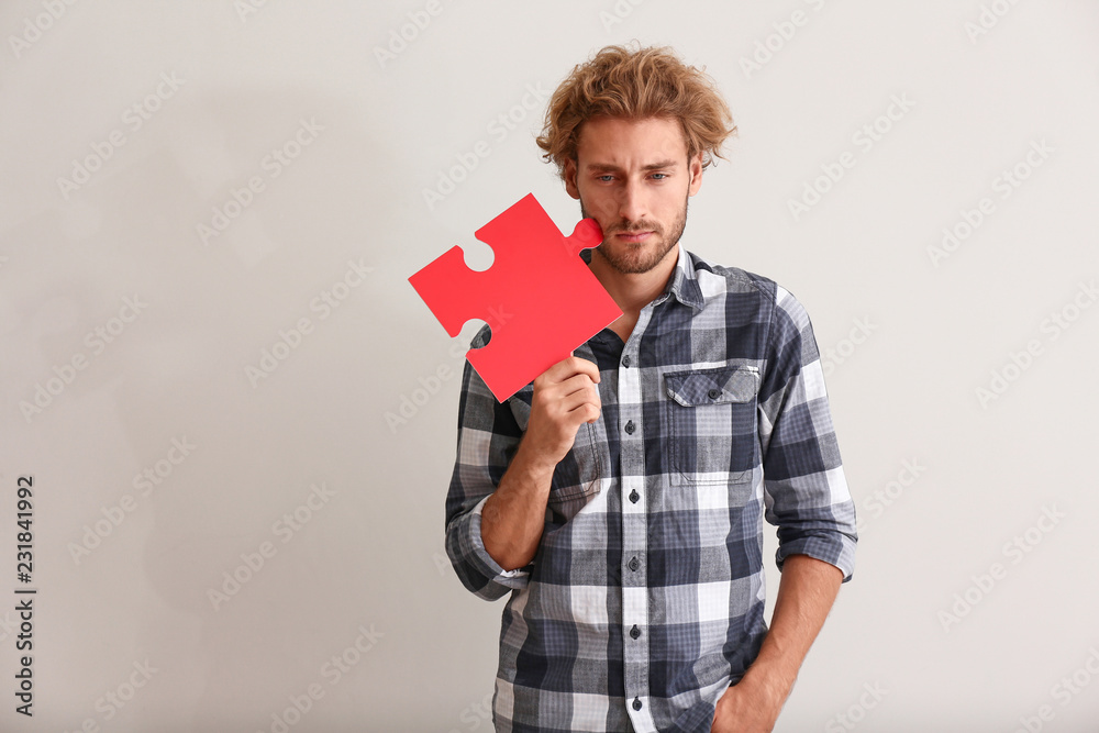 Thoughtful young man with piece of jigsaw puzzle on light background ...