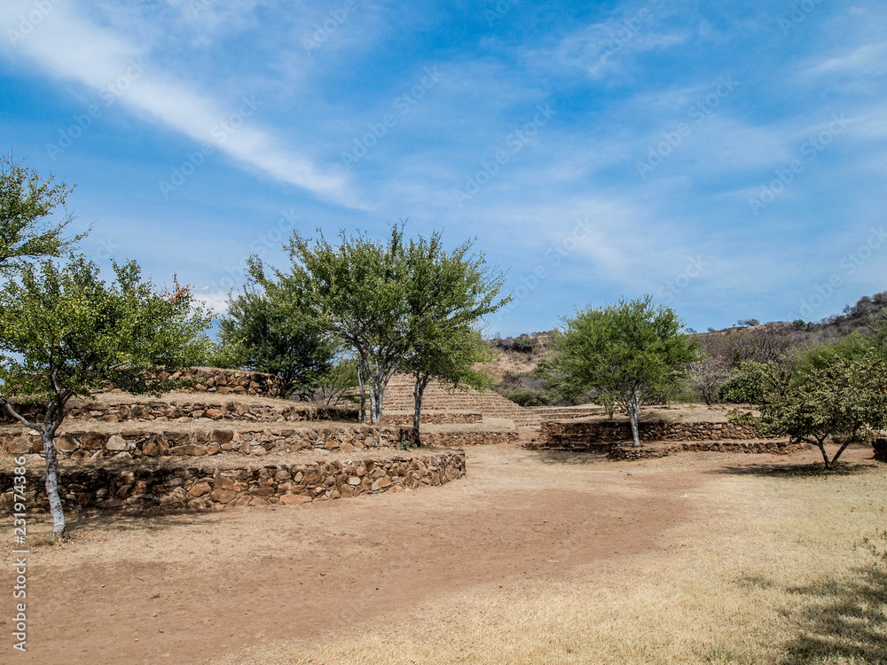 Small circular pyramids, green trees against blue sky, Guachimontones ...
