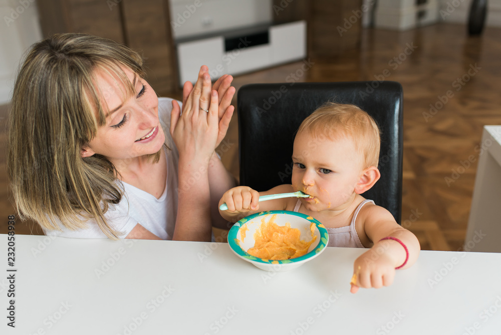 Happy mother smiling and clapping while baby eating healthy baby food ...