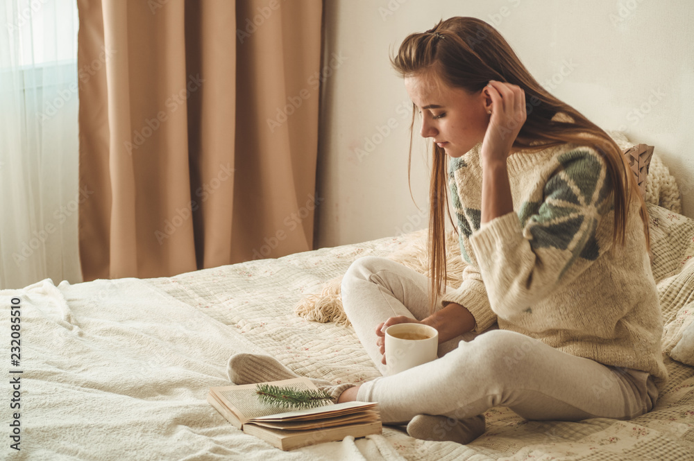 Cozy home. Beautiful girl is reading a book on the bed. Good morning ...