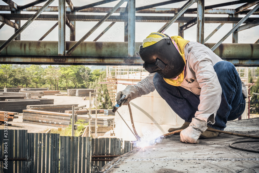 Industrial welder wearing safety helmet welding roof top boiler ...