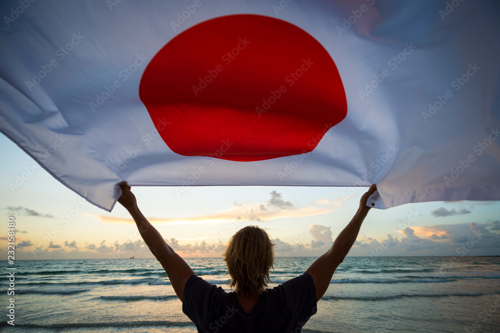 Silhouette of man holding Japanese flag in front of soft sunrise sky at ...