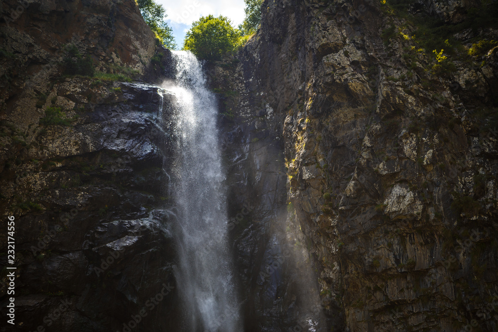 A high waterfall with white splashes of water descends from the ...