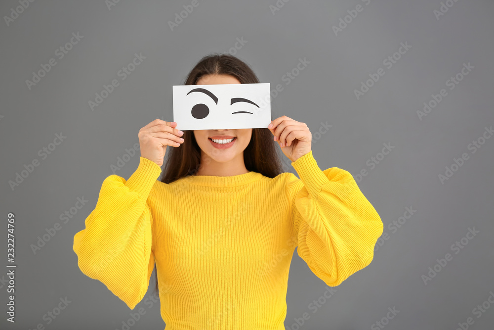 Emotional young woman hiding face behind sheet of paper with drawn eyes ...