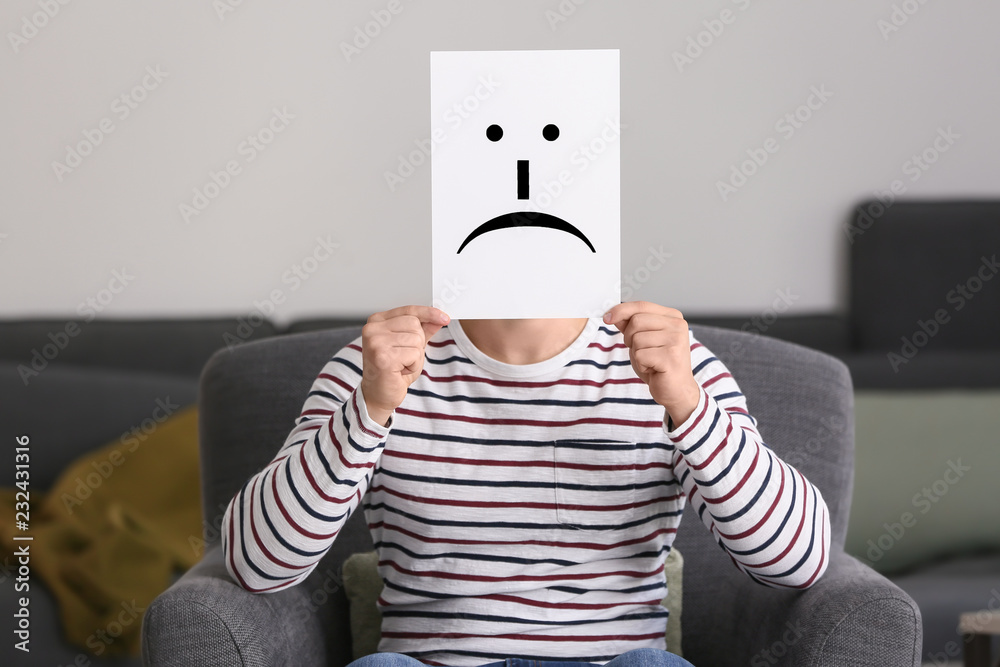 Young man hiding face behind sheet of paper with drawn emoticon while ...