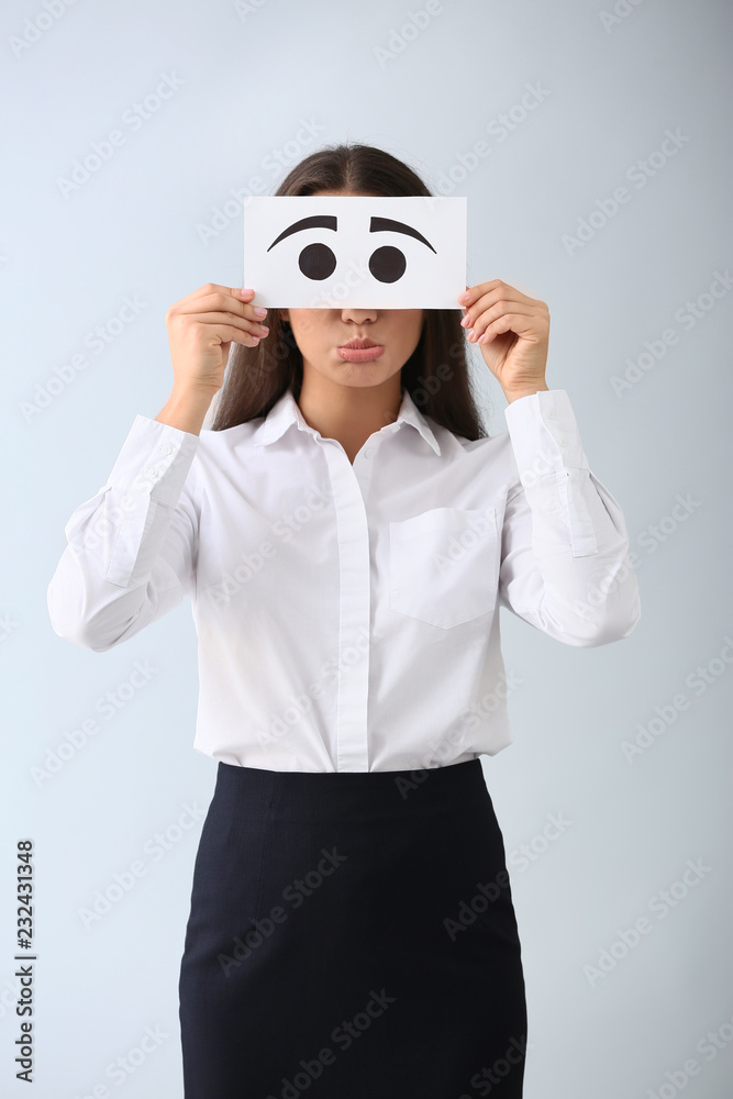 Emotional young woman hiding face behind sheet of paper with drawn eyes ...