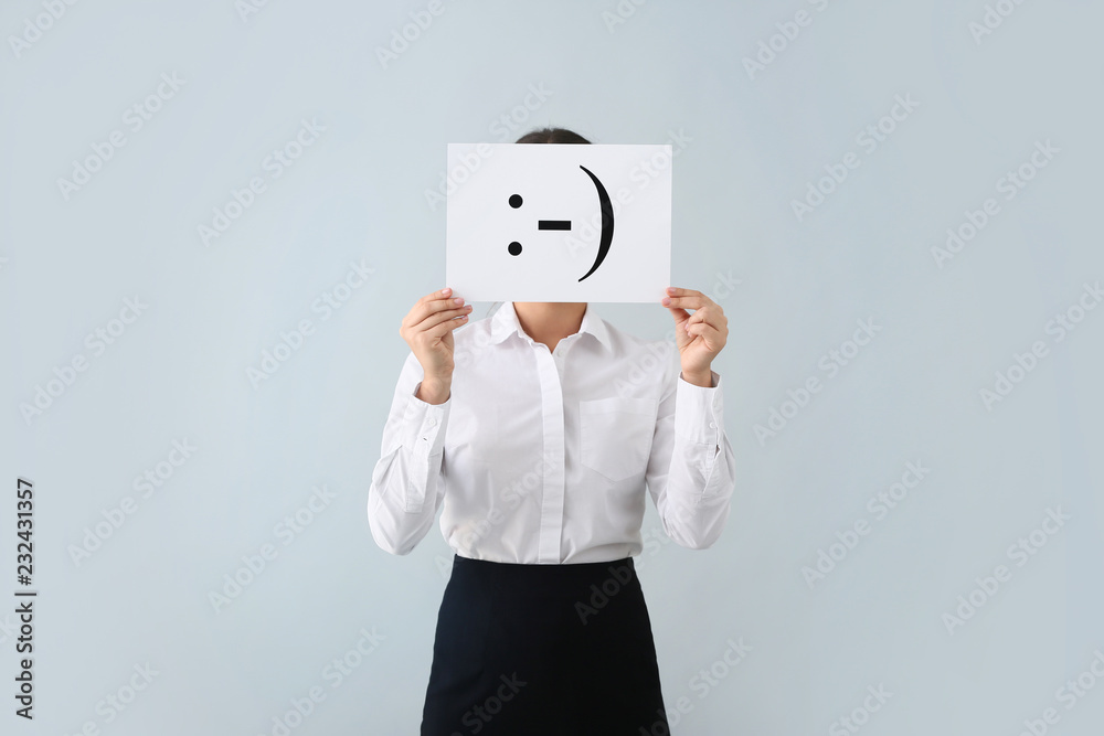 Young woman hiding face behind sheet of paper with drawn emoticon on ...