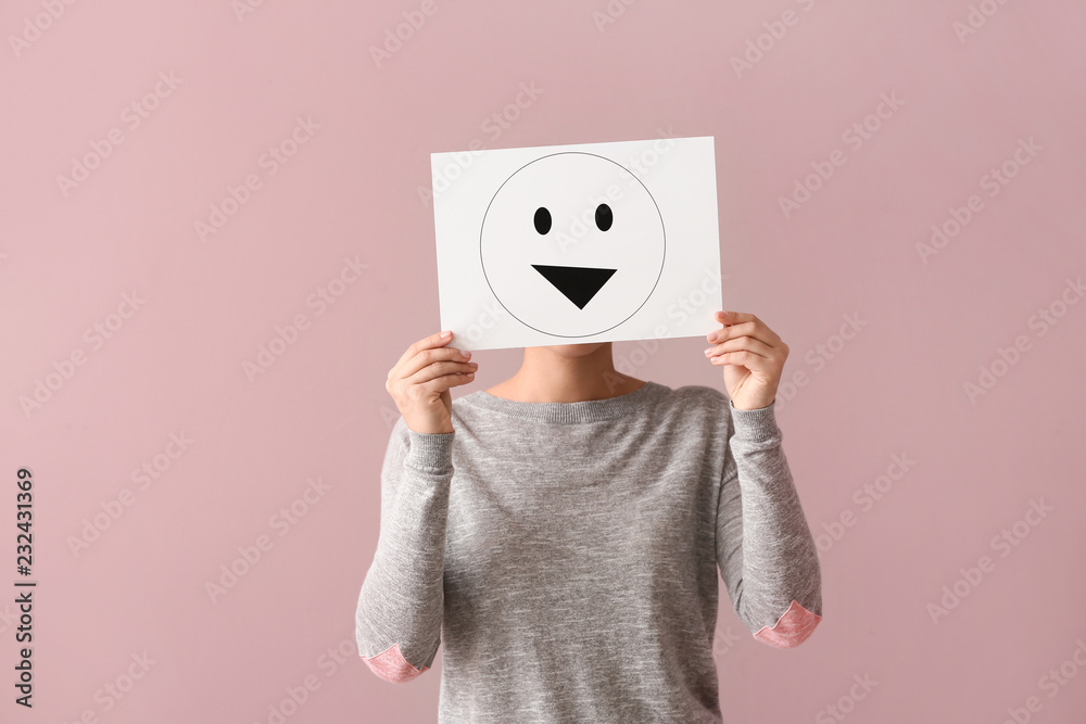 Young woman hiding face behind sheet of paper with drawn emoticon on ...