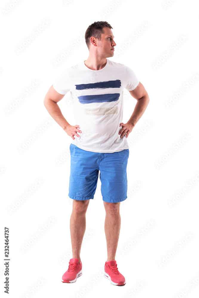 Serious young sporty man with arms on hips looking away over the ...