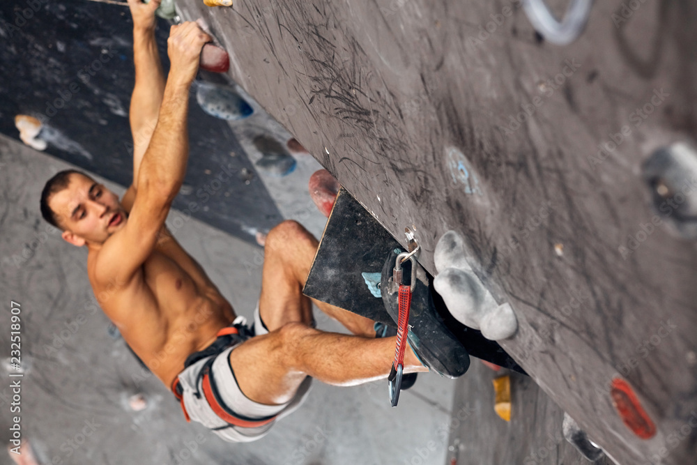 Athletic shirtless man bouldering at an indoor climbing centre ...